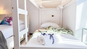 Quarto com beliche, cama branca, cobertor verde e toalha enrolada com fita azul.