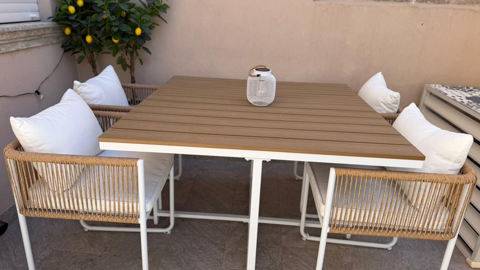 Uma mesa de madeira com almofadas brancas, rodeada por cadeiras de vime.