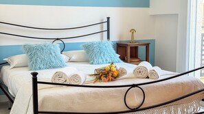 Cama com estrutura metálica, almofadas macias azuis e toalhas dobradas.