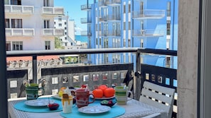 Varanda com mesa posta para refeições, com pratos, copos e uma tigela de frutas.
