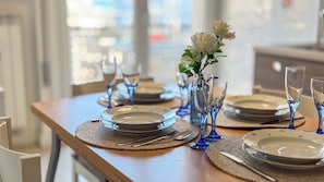 Uma mesa de jantar posta com pratos, talheres e copos de vidro azul, com um vaso de flores brancas ao centro.