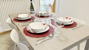 Mesa de jantar posta com pratos, talheres e copos de vinho, com uma garrafa de vinho e um tapete decorativo.