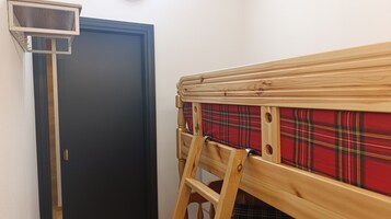Um quarto com uma porta escura, um banco de madeira com almofada xadrez e uma pequena prateleira acima do banco.
