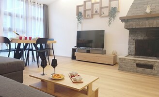 Uma sala de estar moderna com televisão de tela plana, lareira, área de refeições com cadeiras e uma mesa de centro com lanches.