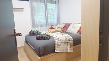 Uma cama com roupa de cama cinza, um cobertor branco fofo e toalhas enroladas com fitas verdes.