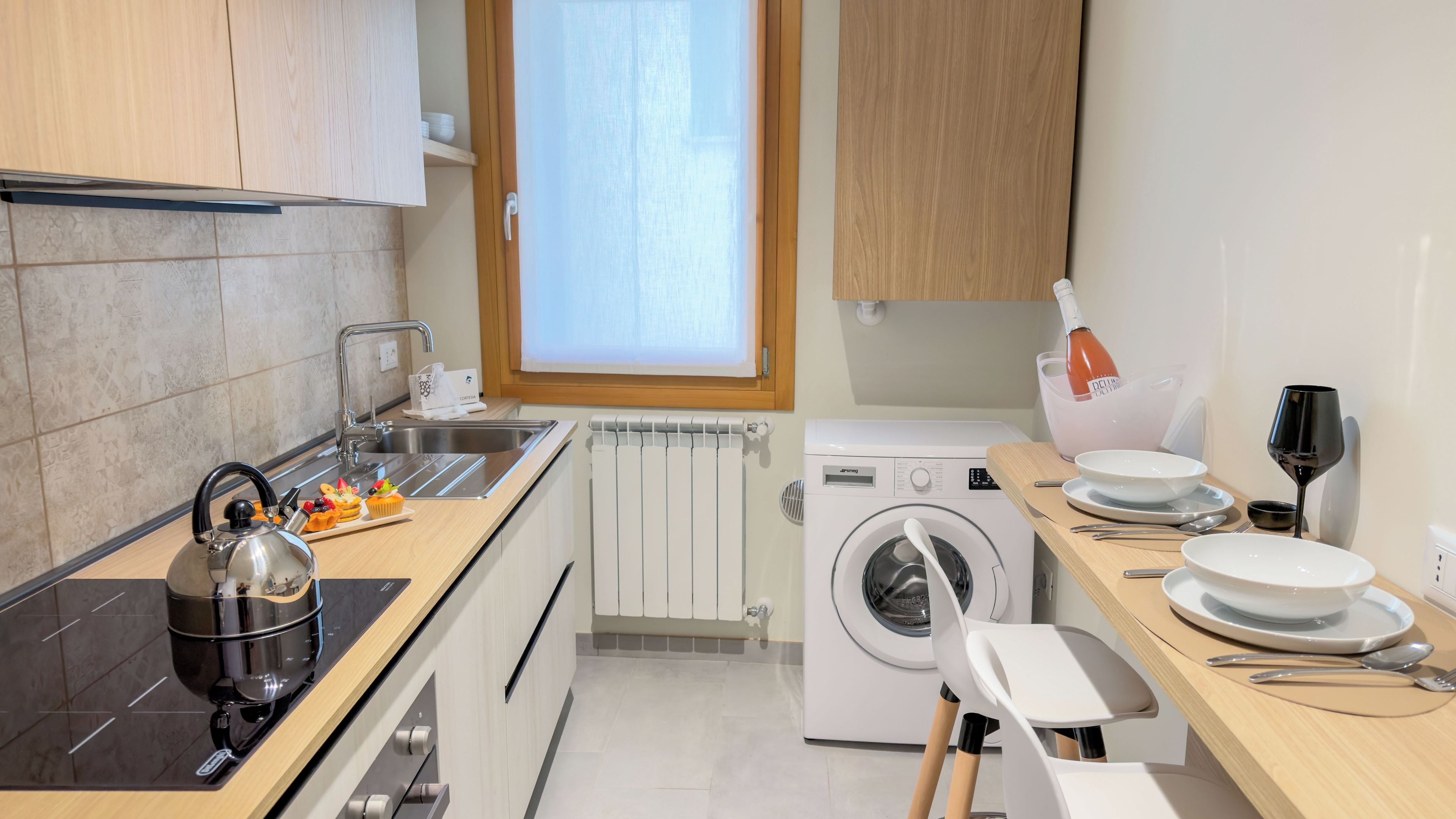 Uma cozinha moderna com chaleira, máquina de lavar roupa e área de refeições com pratos e talheres.