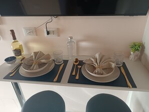 Uma mesa de jantar bem posta, com pratos, talheres, copos, uma garrafa e uma pequena planta.