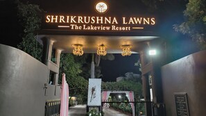 Entrada do Shrikrushna Lawns The Lakeview Resort, com uma placa sobre o portão, lustres e um caminho que leva à propriedade.