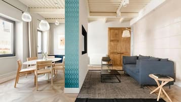 Uma sala de estar moderna com área de jantar, piso de madeira e uma grande janela que proporciona iluminação natural.