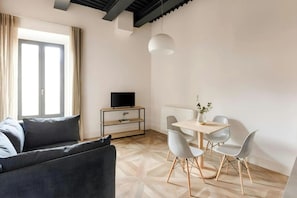 Uma sala de estar moderna com sofá, TV em um suporte de madeira, mesa de jantar com cadeiras e uma luminária pendente.