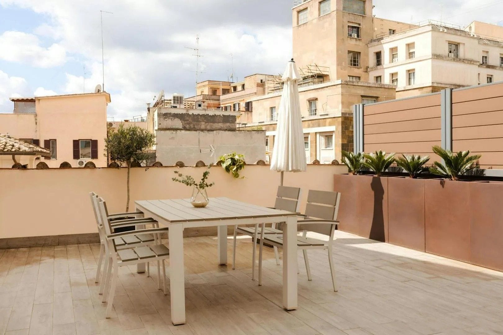 Pátio externo com mesa e cadeiras, cercado por um muro baixo com plantas.