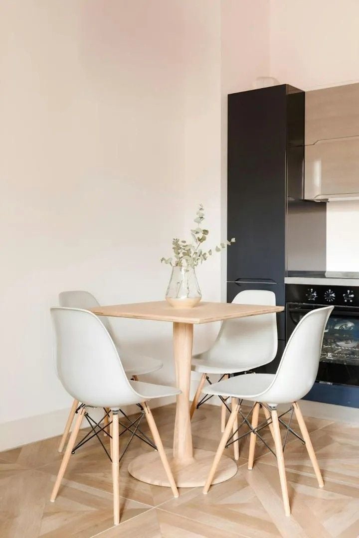 Uma cozinha moderna com uma mesa de madeira redonda, cadeiras brancas e um vaso com flores.