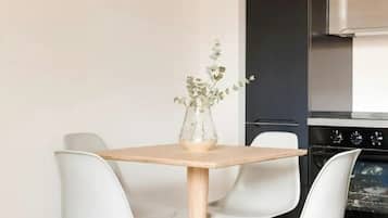 Uma cozinha moderna com uma mesa de madeira redonda, cadeiras brancas e um vaso com flores.