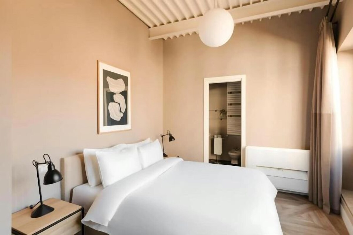 Quarto de hotel com cama, mesa de cabeceira, abajur e uma obra de arte na parede.