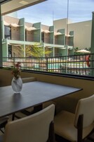 Uma área de refeições com mesa e cadeiras, um vaso com flores e vista para um edifício com várias varandas.