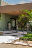 Entrada moderna de um edifício com varanda coberta, vasos decorativos grandes e escadaria que leva à entrada.