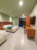 Quarto de hotel com cama, escrivaninha, televisão e porta corrediça para um banheiro.