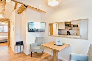 Um espaço compacto com cozinha compacta, televisão de tela plana na parede e uma pequena mesa com cadeira.