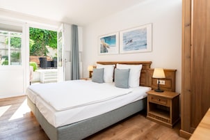 Quarto de hotel com uma cama grande, duas mesas de cabeceira com abajures, um guarda-roupa de madeira e duas imagens emolduradas na parede.