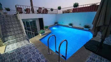 Piscina no terraço com estrutura de vidro, rodeada por plantas em vasos e móveis de exterior.