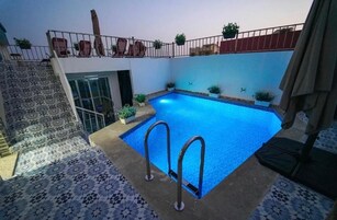 Piscina no terraço com estrutura de vidro, rodeada por plantas em vasos e móveis de exterior.