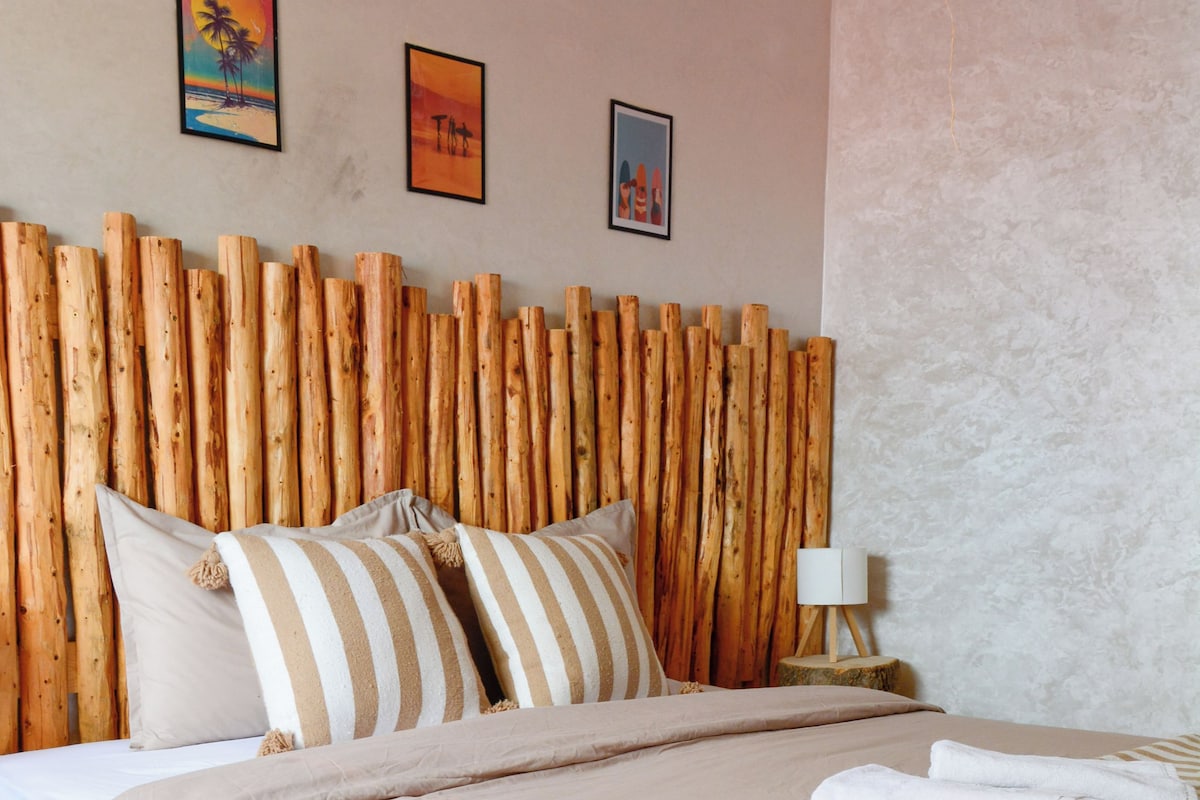 Cama com roupa de cama listrada, cabeceira de madeira e parede com duas quadros.