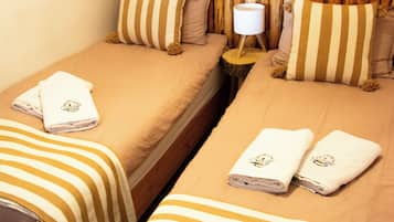 Quarto de hotel com duas camas, cada uma com roupa de cama e almofadas listradas, mesa de cabeceira com abajur e cabeceira de madeira.