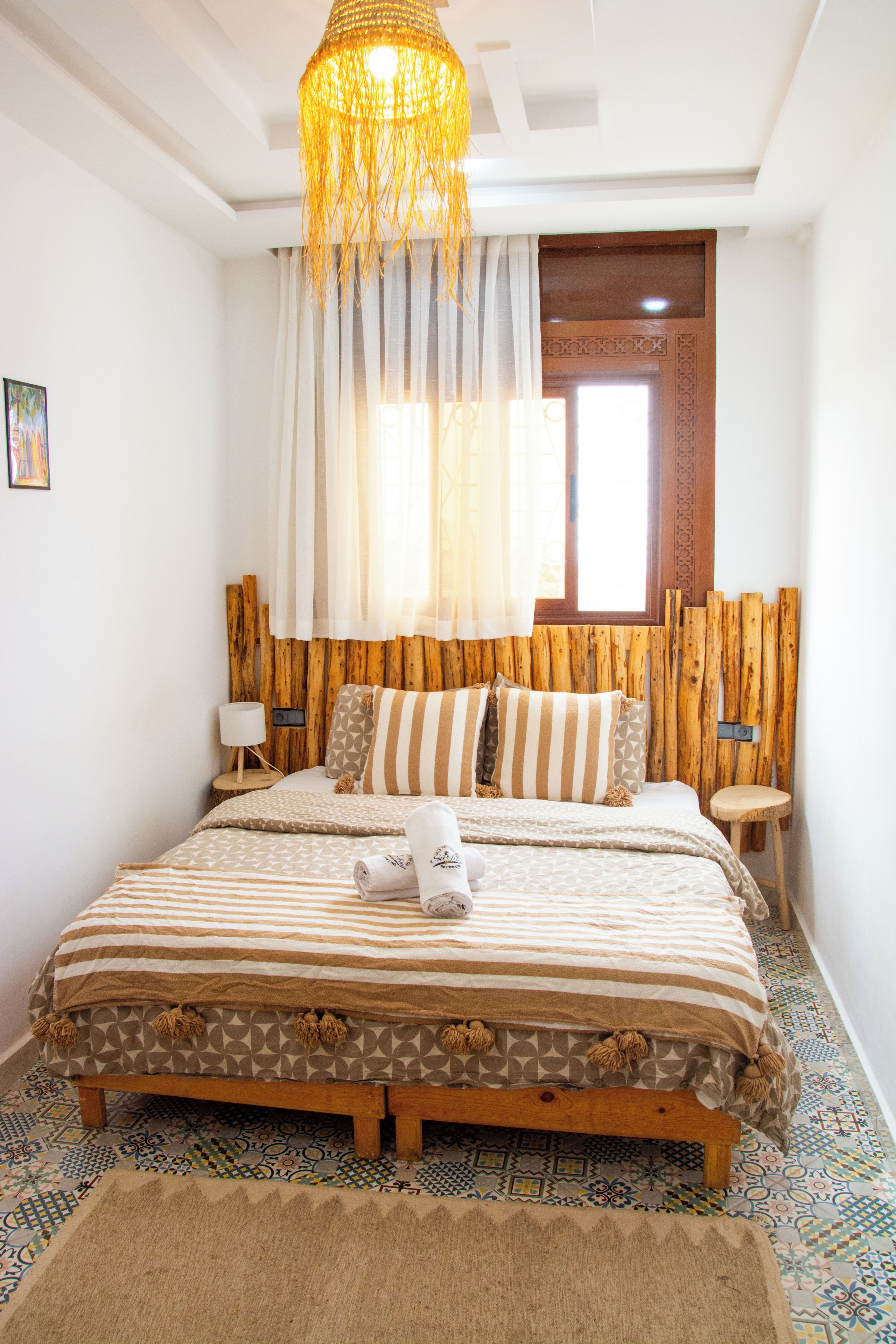 Quarto com cama, luminária pendente, janela e piso estampado.