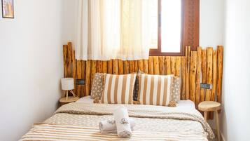 Quarto com cama, luminária pendente, janela e piso estampado.