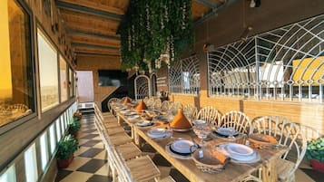 Uma longa mesa de jantar com cadeiras, chão xadrez e folhagem pendente.