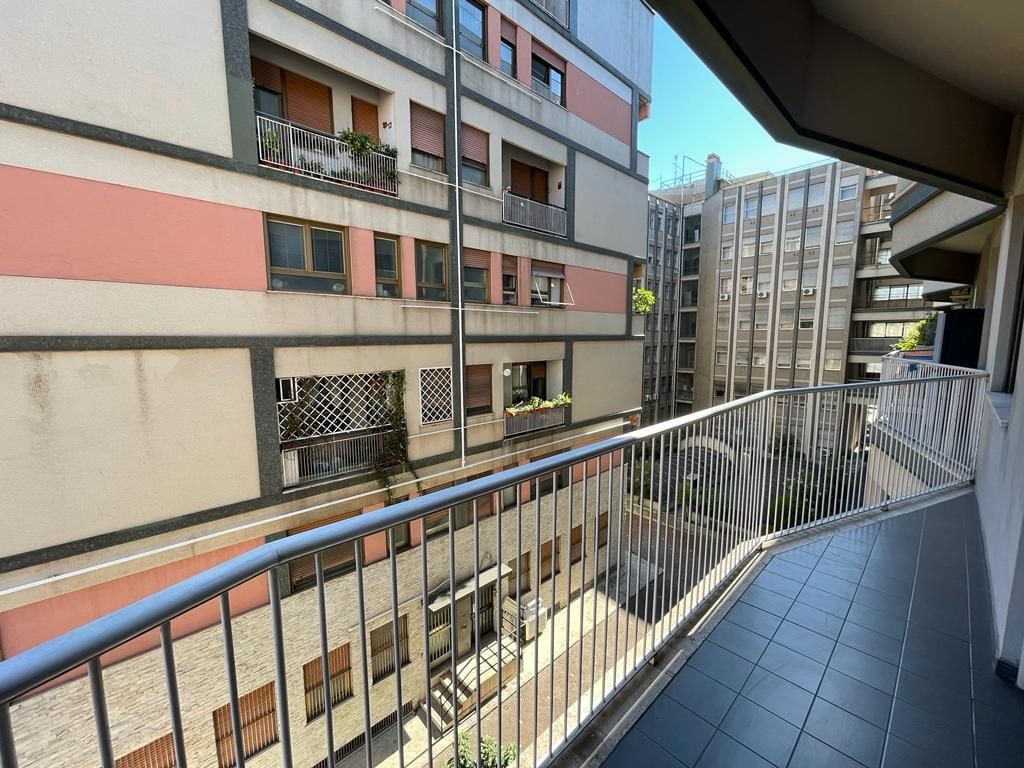 Um edifício residencial com vários andares, varandas, piso de azulejos e guarda-corpo de metal.