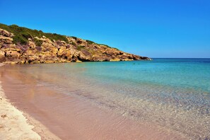 Uma praia com águas cristalinas, falésias rochosas e vegetação.