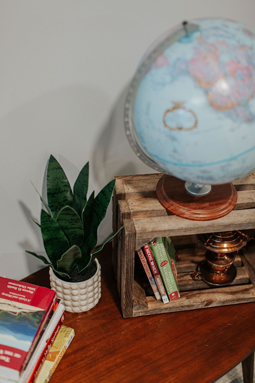 Uma mesinha de madeira com um globo, uma planta em vaso e uma pilha de livros.