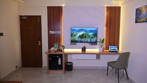Bancada de recepção de hotel com televisão de tela plana, máquina de café, laptop e lixeira.