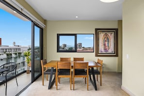 Uma área de refeições com mesa e cadeiras, uma janela grande com vista para a cidade e uma obra de arte emoldurada na parede.