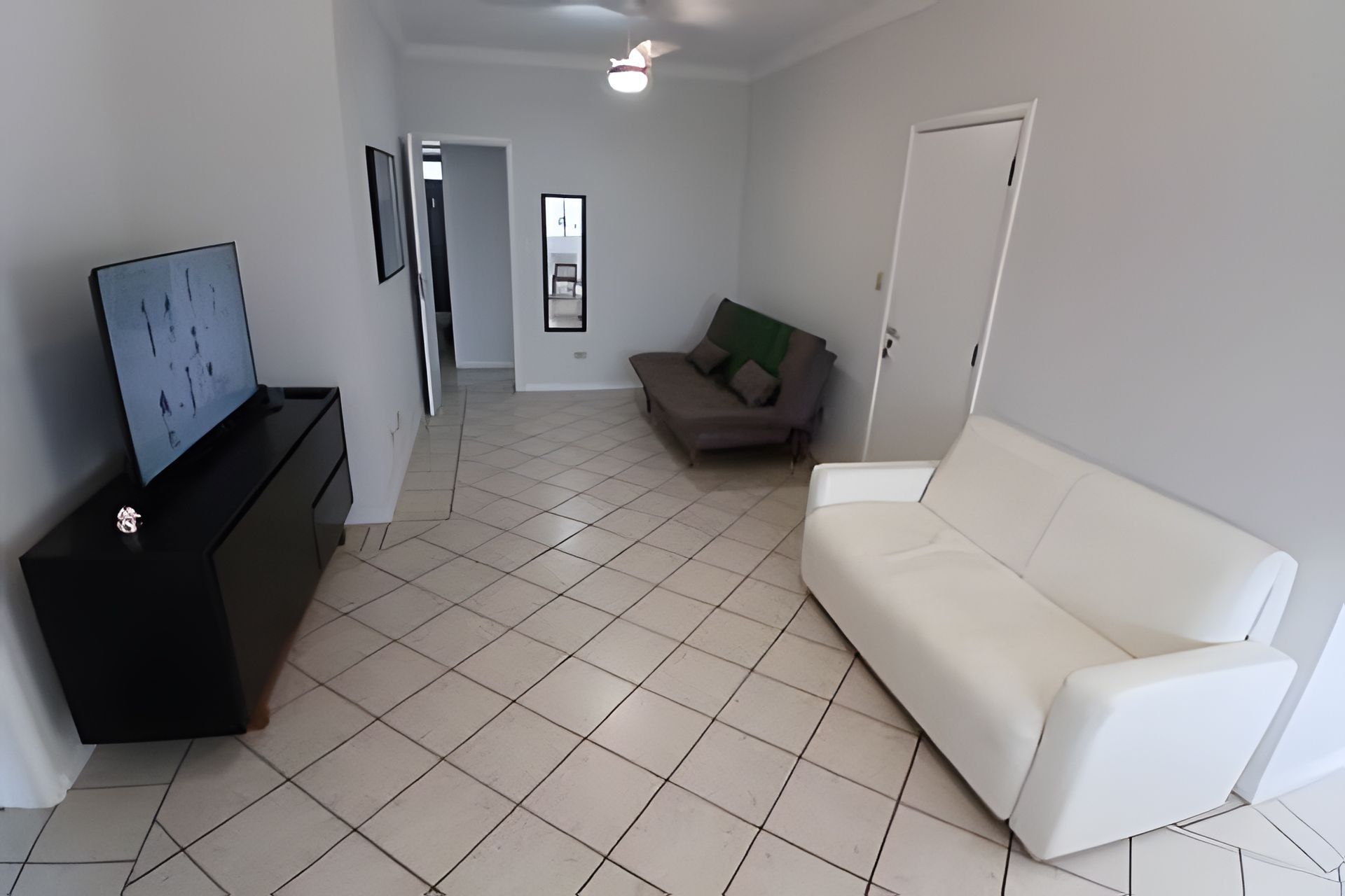 Uma sala de estar ampla com um sofá branco, um armário de madeira escura com uma TV de tela plana e piso ladrilhado.