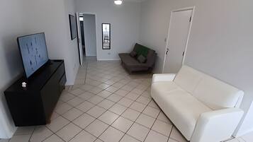 Uma sala de estar ampla com um sofá branco, um armário de madeira escura com uma TV de tela plana e piso ladrilhado.