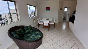Uma sala de estar moderna com uma janela grande, uma área de jantar com mesa e cadeiras, e uma cozinha.