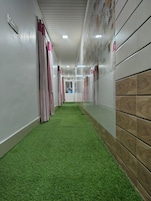 Corredor com carpete verde artificial, paredes brancas e detalhe em painel de madeira.