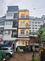 Um edifício de vários andares com uma placa 'MDFAMMA' no último andar, uma entrada visível e uma escadaria que leva à entrada.