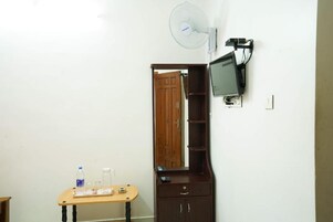 Quarto com armário de madeira, televisão na parede e uma mesinha com garrafa e copos.