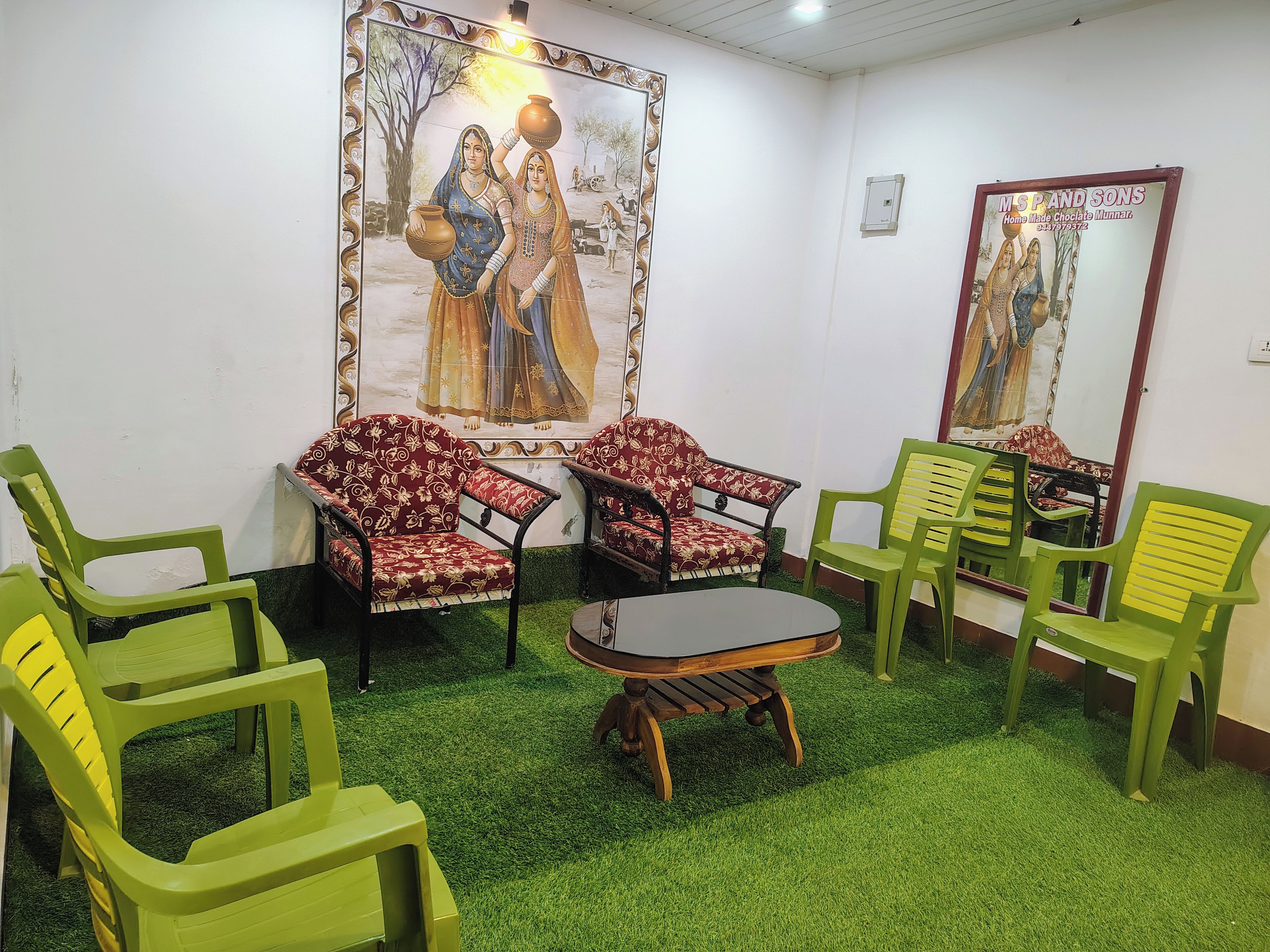 Um quarto com cadeiras de plástico verde, uma mesa de madeira e um mural na parede.