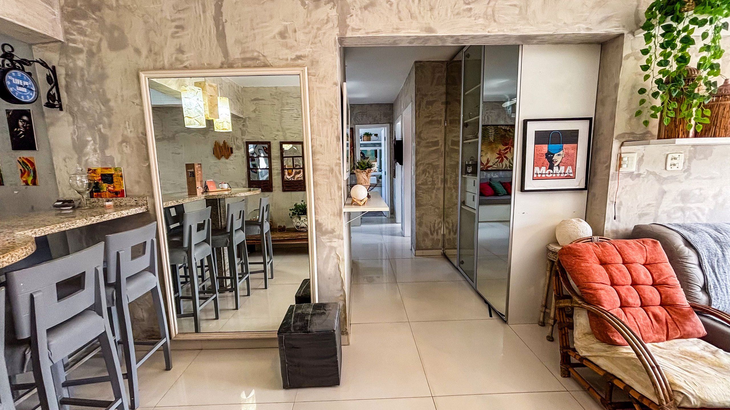 Uma cozinha moderna com área de bar, espaço de jantar com cadeiras, um sofá e um espelho refletindo o ambiente.