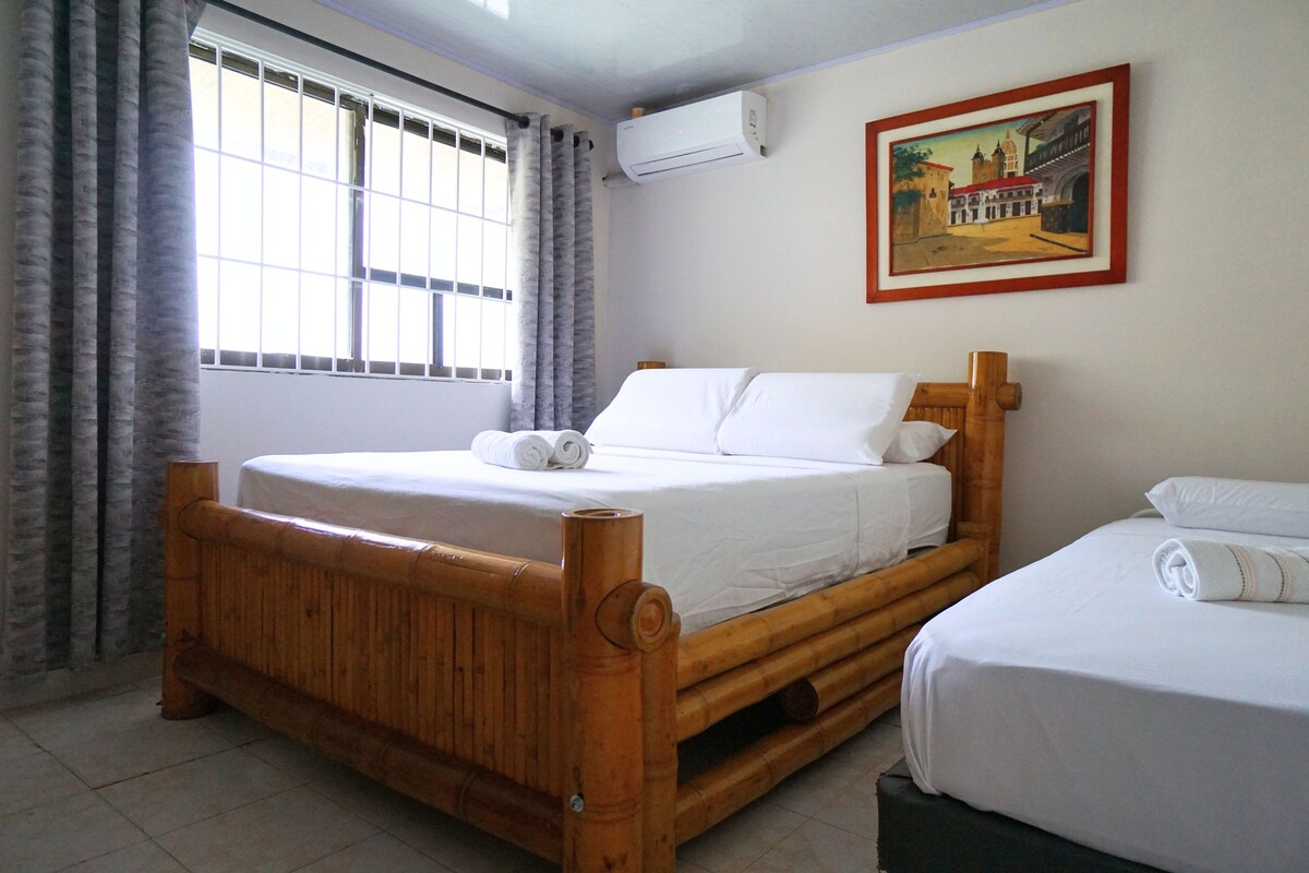 Quarto com cama de madeira, janela com cortinas, ar condicionado e um quadro na parede.