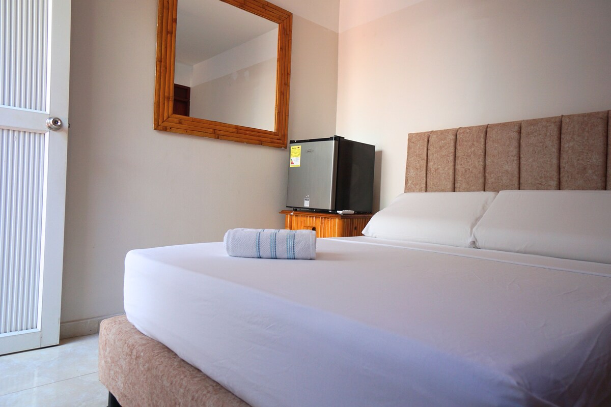 Quarto de hotel com uma cama, televisão sobre um suporte de madeira, um espelho na parede e uma porta.