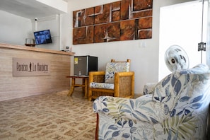 Uma área de recepção com um balcão de madeira, televisão, obra de arte na parede e um ventilador.