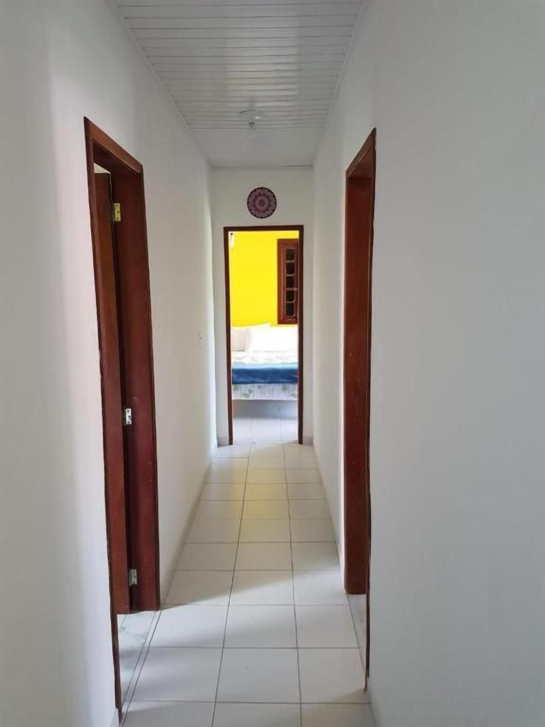 Corredor estreito com piso de azulejos brancos e portas de madeira em ambos os lados.