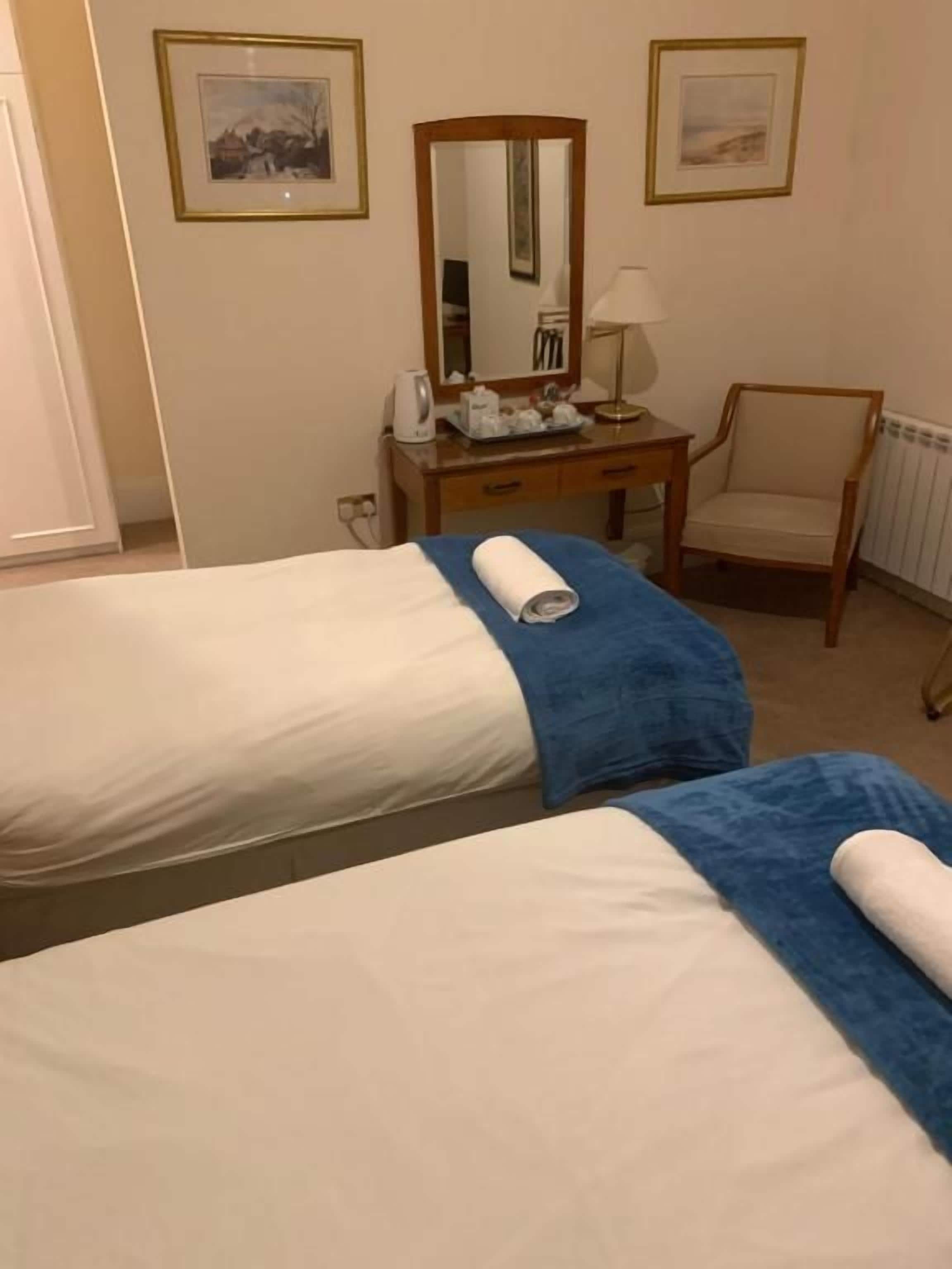 Quarto de hotel com duas camas, uma mesa com abajur e uma cadeira.