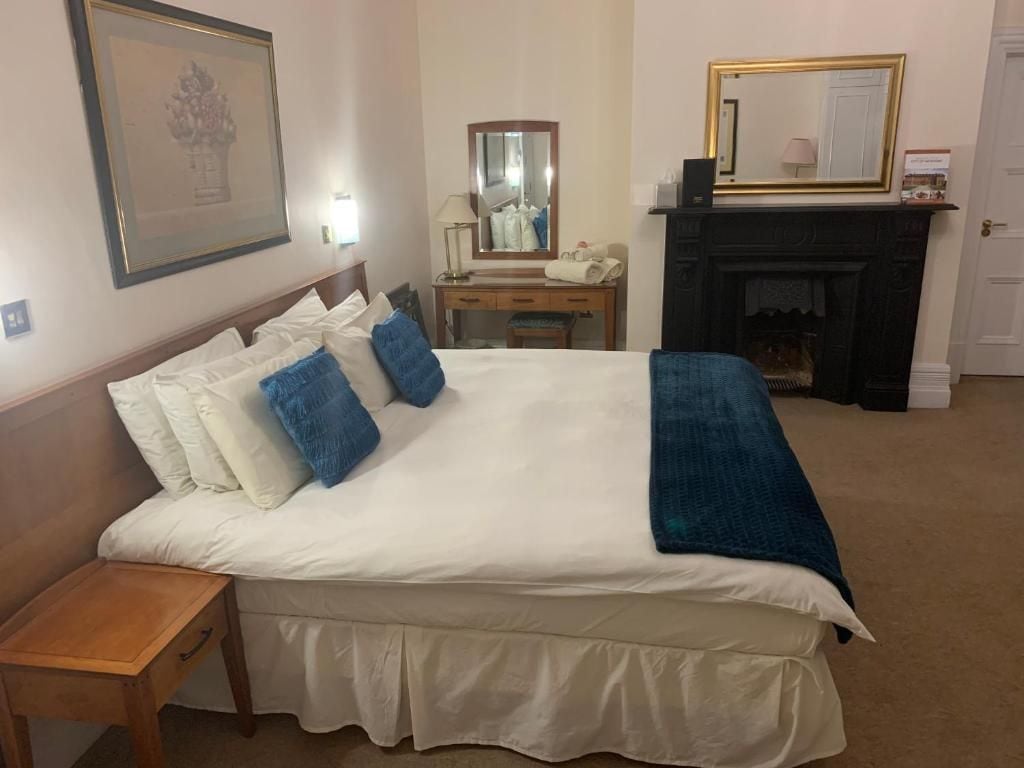 Quarto de hotel com cama, mesa de cabeceira, cômoda, espelho, lareira e arte emoldurada na parede.