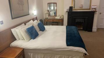 Quarto de hotel com cama, mesa de cabeceira, cômoda, espelho, lareira e arte emoldurada na parede.
